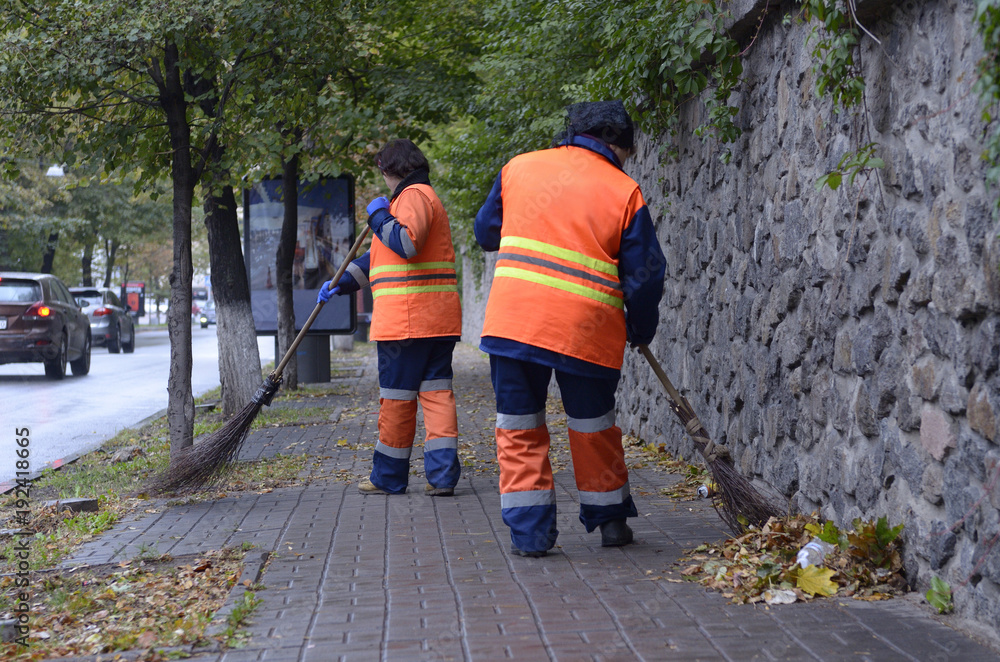 Municipal street sweepers sweeping leaves with broom tools on a street ...