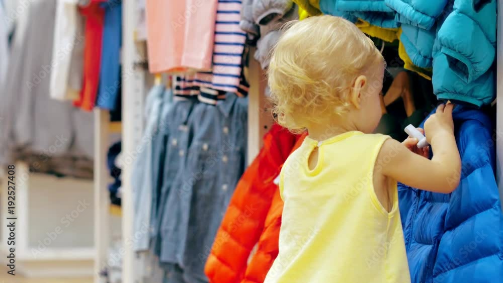 Little girl touching clothes in childrens clothing store during family ...