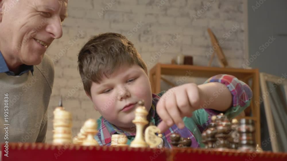 Grandfather and grandson plays chess. Elderly man teaches chess to play ...