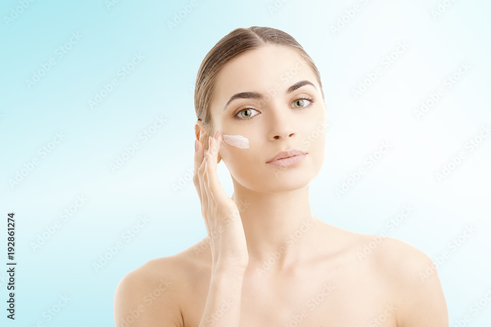 Studio shot of beautiful young woman applying moisturizer cream onto ...