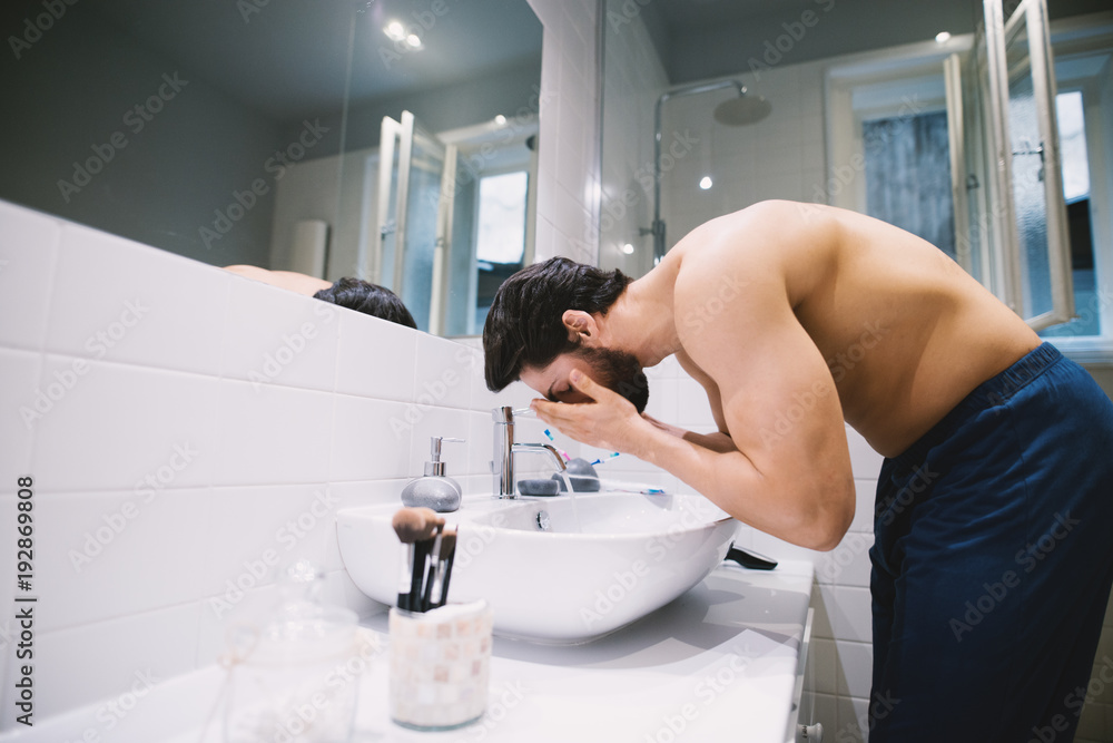 Attractive man washing his face in the bathroom sink getting ready for ...