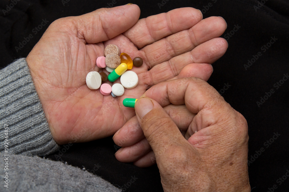 An elderly man holds a lot of colored pills in old hands on a dark ...