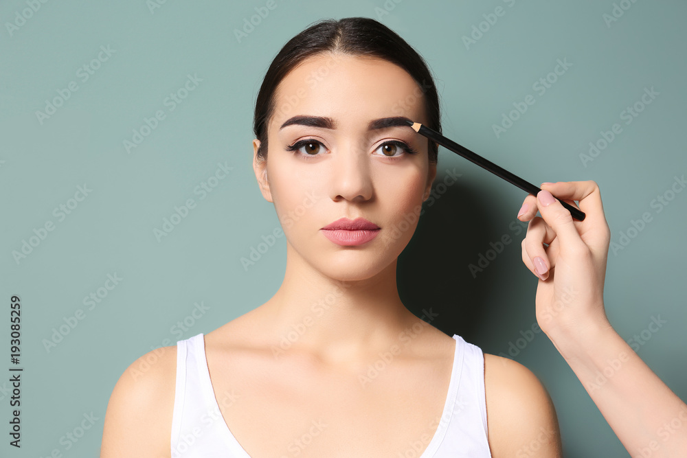 Young woman undergoing eyebrow correction procedure on color background ...