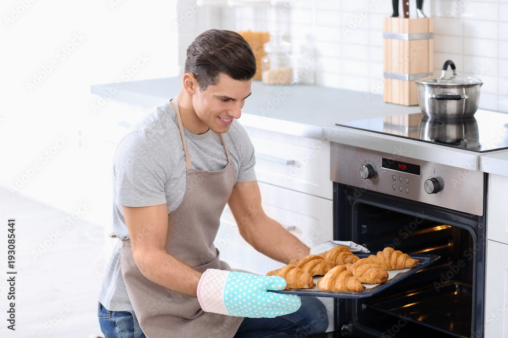 Man taking baking tray with delicious croissants out of electric oven ...