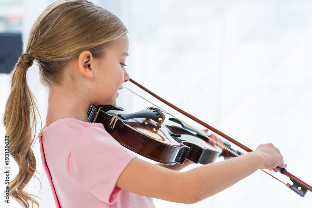 side view of cute little child in pink dress playing violin at home ...