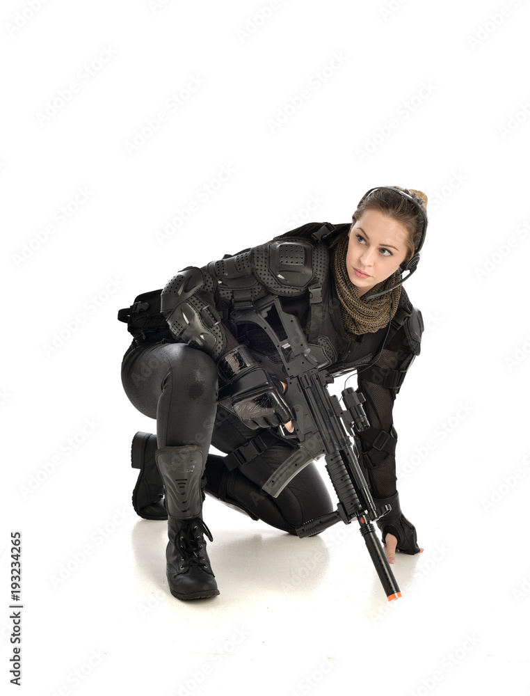 full length portrait of female wearing black tactical armour, crouching ...