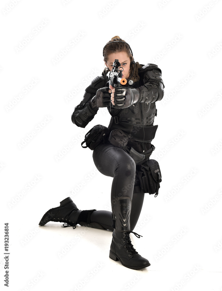 full length portrait of female wearing black tactical armour, crouching ...
