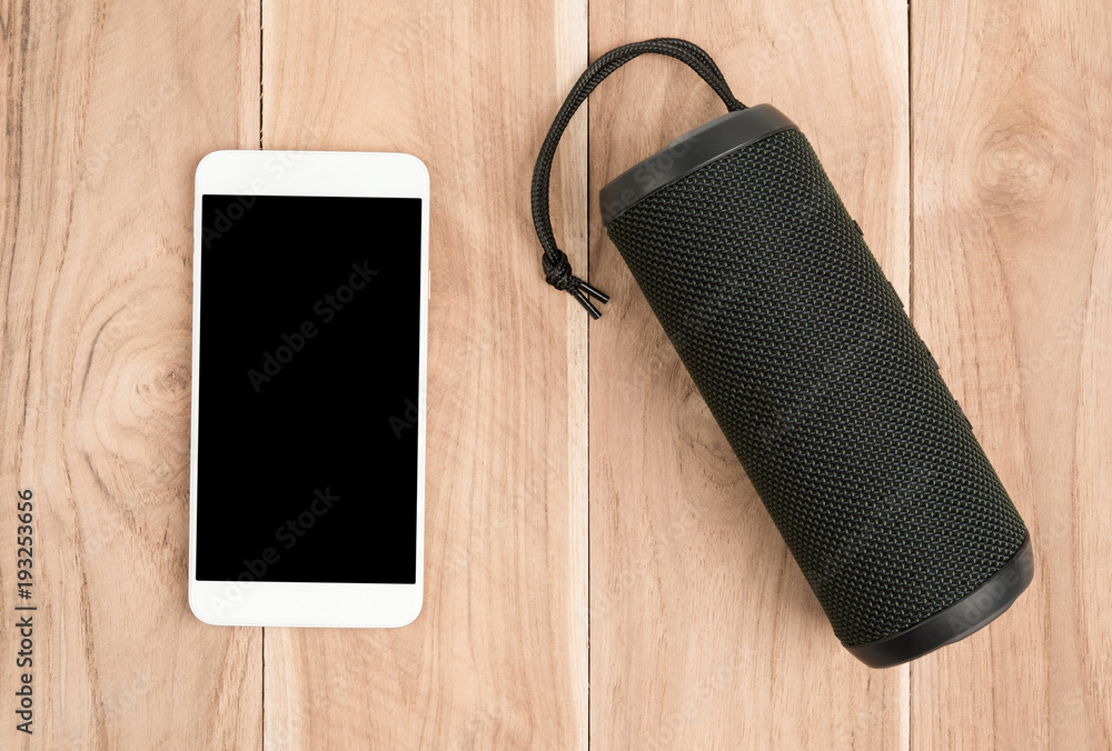 White mobile smart phone with bluetooth speaker on wooden desk ...