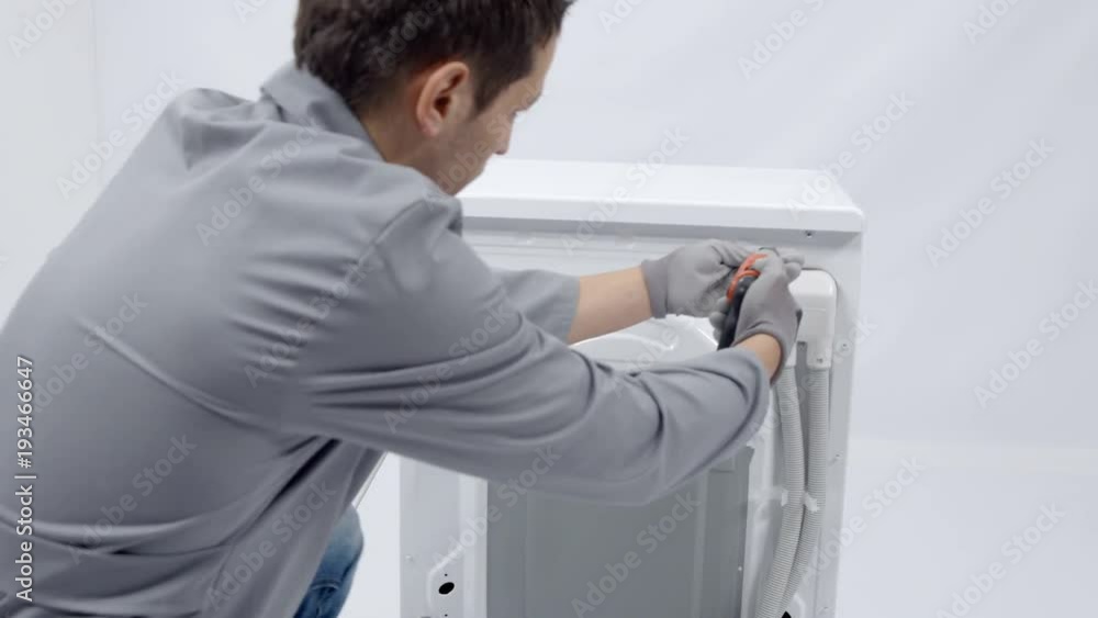 A repairman is using a drill to take out screws on the back of the ...