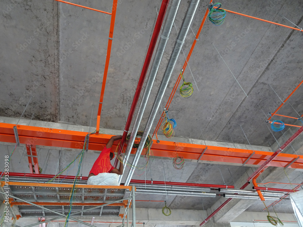 Construction workers installing electrical cable tray and doing wiring ...