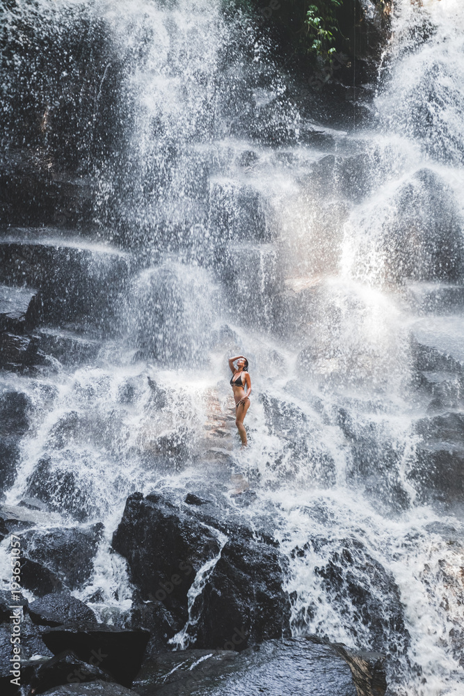 Woman enjoying under stream of big and beautiful cascade waterfall ...