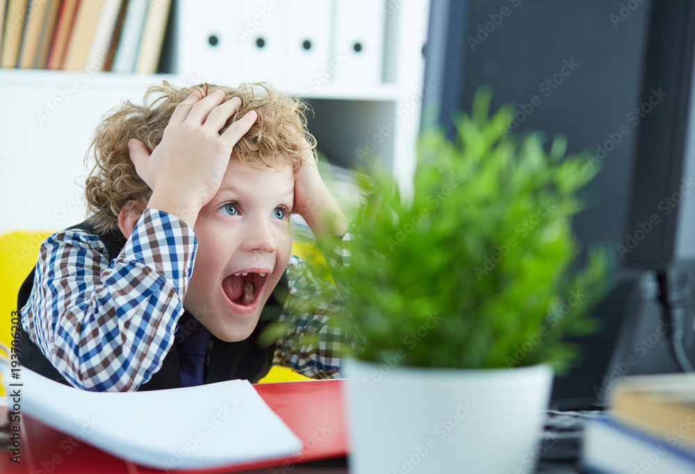 Little Caucasian curly boy looks at the computer screen and screams ...