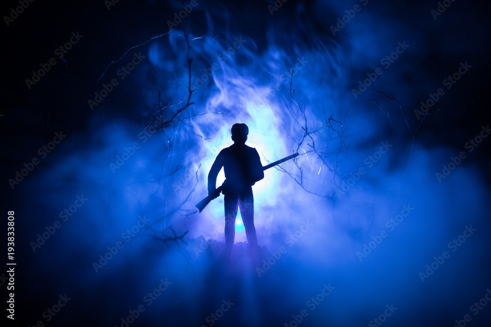 Man with riffle at spooky forest at night with light, or War Concept ...