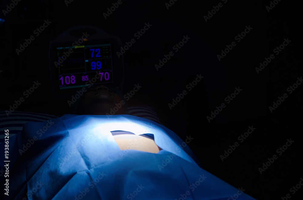 soft focus image of patient on bed with ECG/EKG monitor showing heart ...