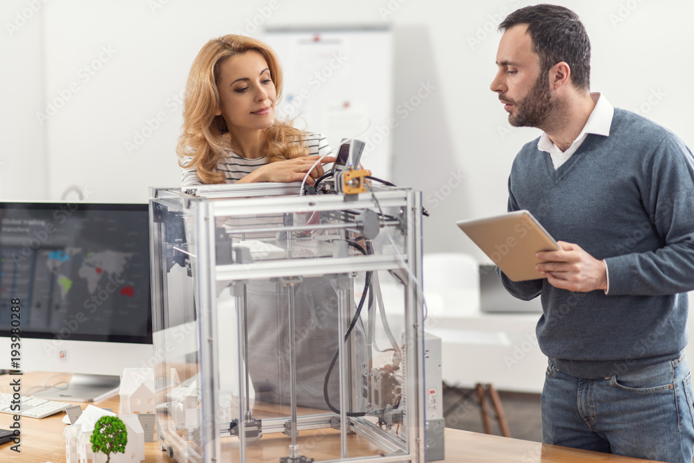 Vital improvements. Pleasant young colleagues updating the firmware of a 3D printer while the ...