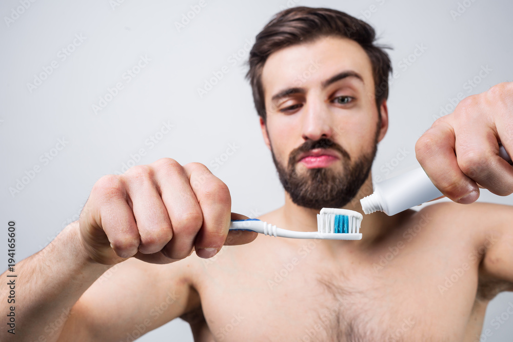Attractive man putting some tooth paste on his tooth brush. He repeats ...