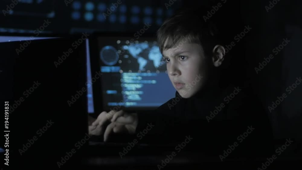 young prodigy boy hacker programmer working at the computer in the data center filled with ...