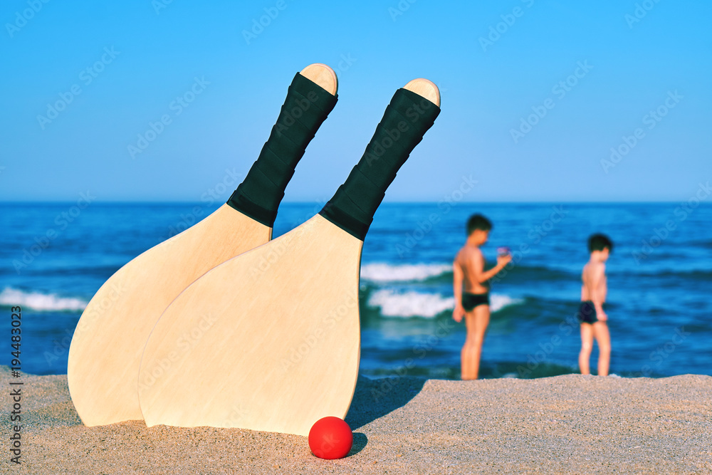 Rockets for playing badminton and a green ball in the sand. Two boys on ...