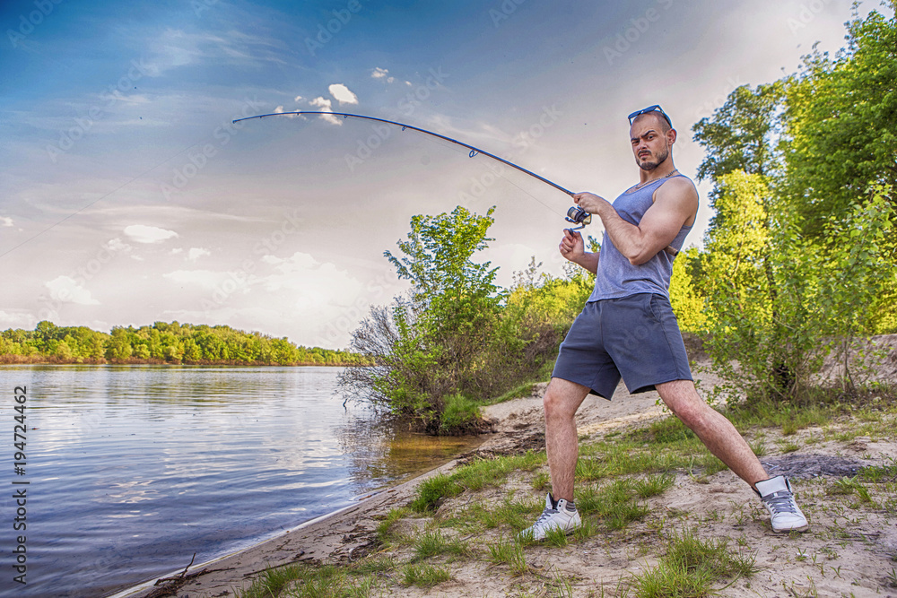 Young handsome brutal caucasian man in casual outfit fishing on a lake ...