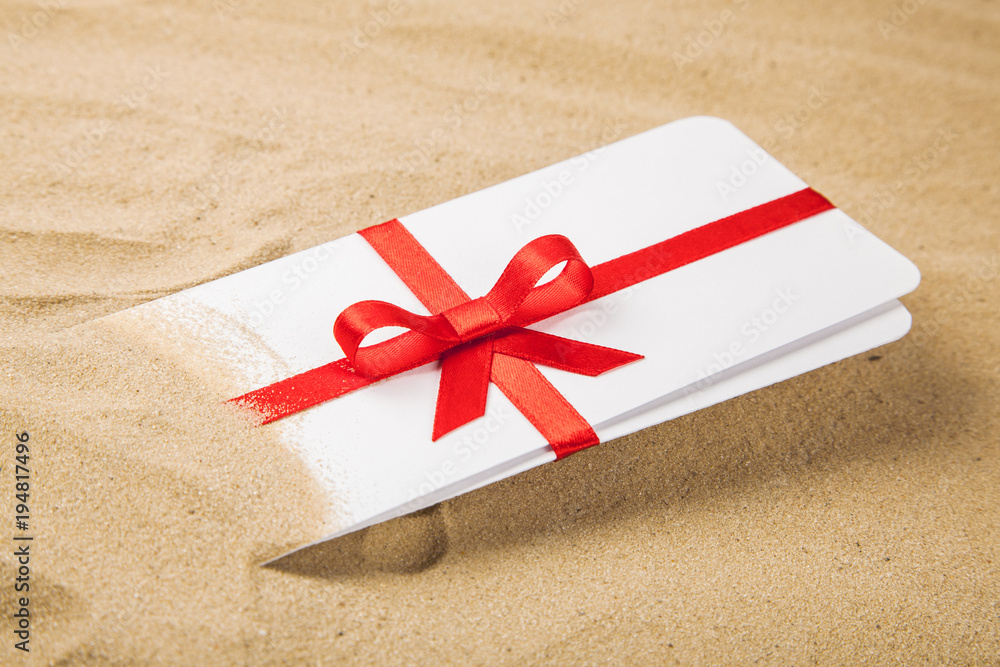 Air tickets as a gift with a red ribbon and bow. Background sand beach ...