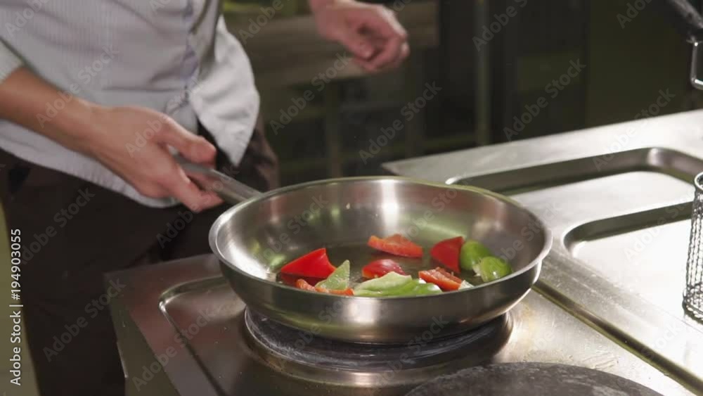 Male cook is frying pepper in oil. He is laying vegetables in red-hot ...