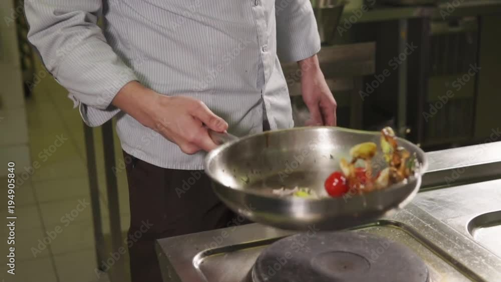 Male cook is masterfully mixing ingredients in a frying pan. He is ...
