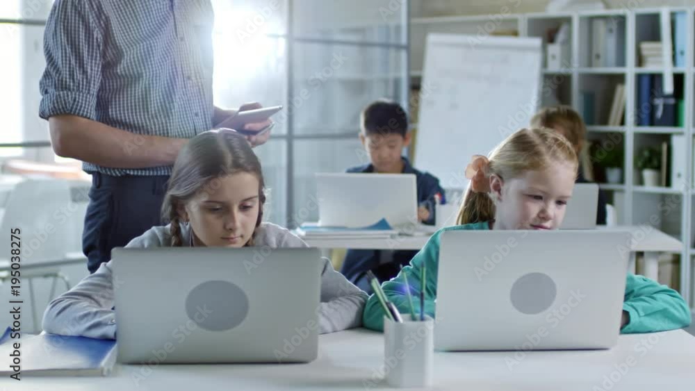 Young male teacher standing and monitoring students' progress while ...