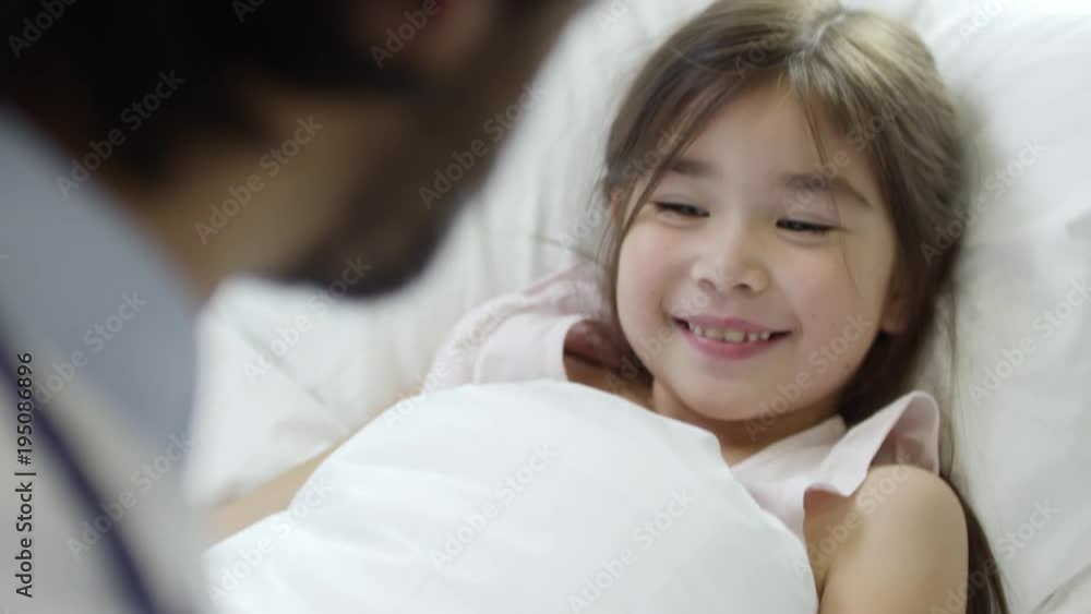 Vidéo Stock Tilt up of smiling little girl lying in hospital bed and ...