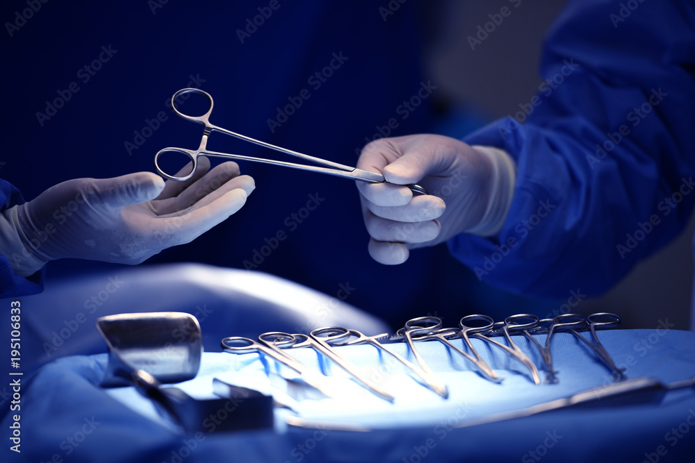 Surgeon hand picking up an instrument from tray of surgical instruments ...
