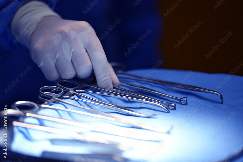Surgeon hand picking up an instrument from tray of surgical instruments ...