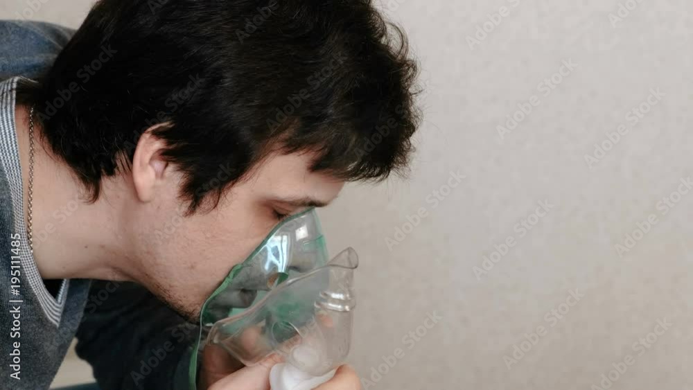 Use nebulizer and inhaler for the treatment. Young man inhaling through ...