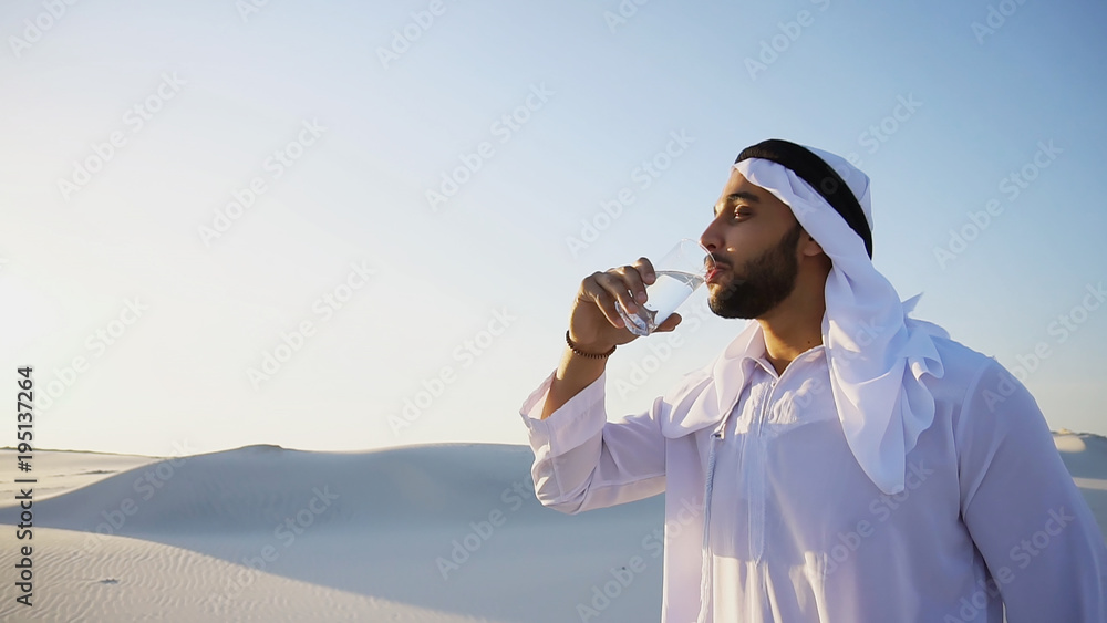 Stately Arab young man quenches thirst with glass of cool water and ...