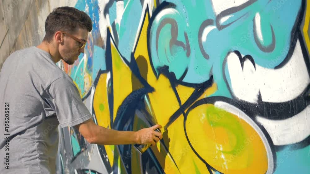 Graffiti artist is painting a black triangle on the yellow letter ...