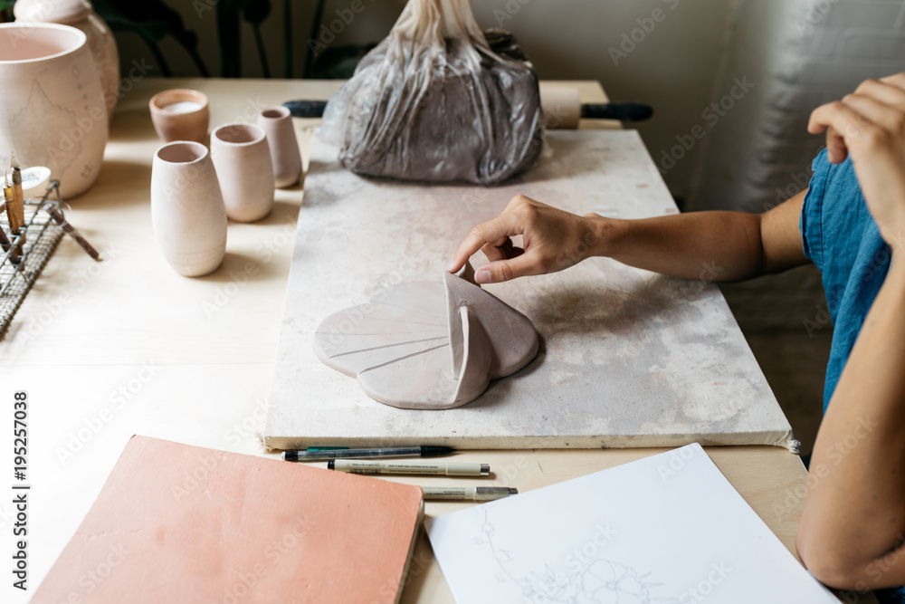female ceramics maker pointing at work in progress pieces on desk in ...