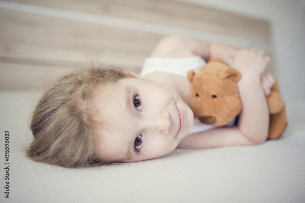 Beautiful and sweet little girl overlie on bed with her toy teddy bear ...