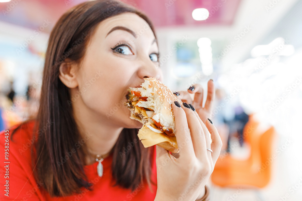 Pretty young funny woman eating hamburger inside in fast-food ...