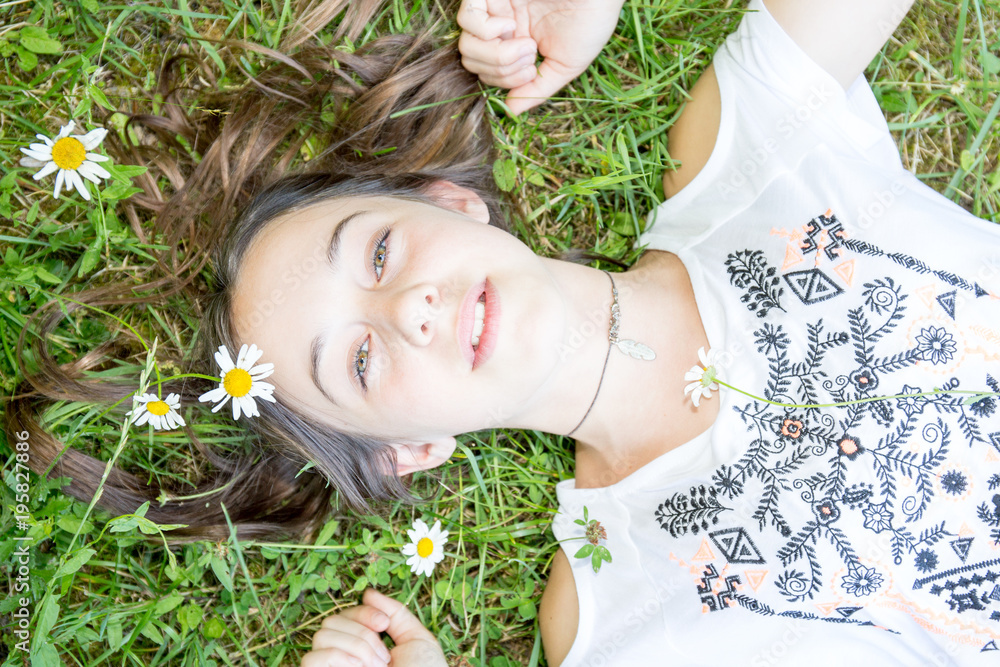 Relaxed young teenage girl lying in grass and flowers with stretched ...