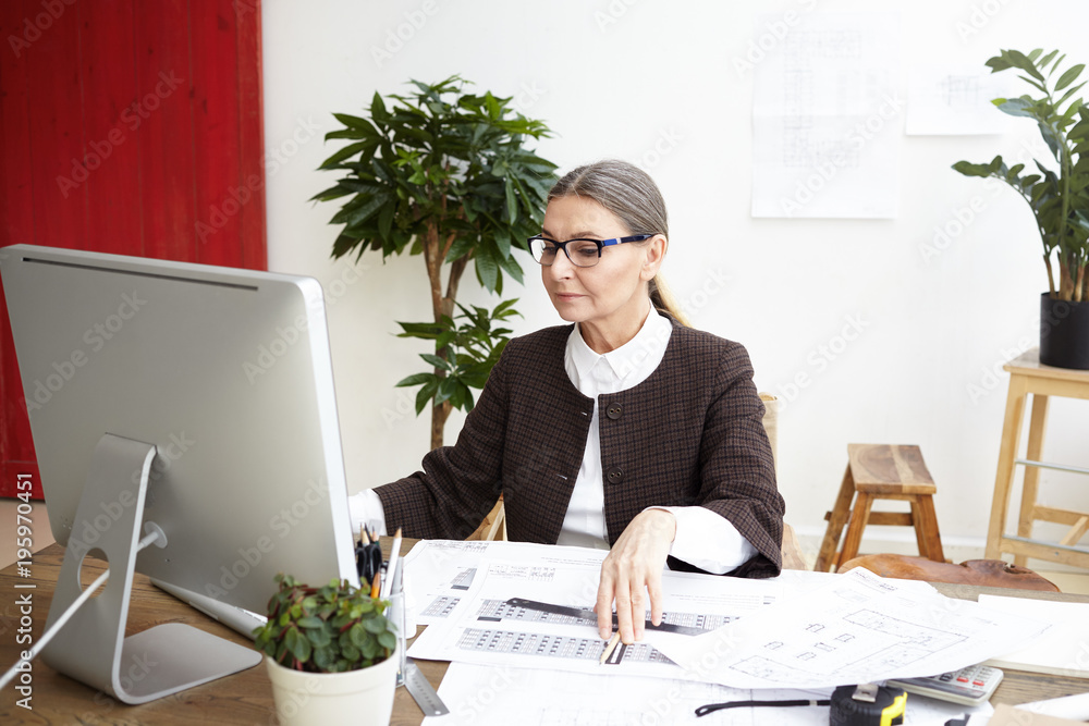 Concentrated mature female architect making drawings, comparing them ...