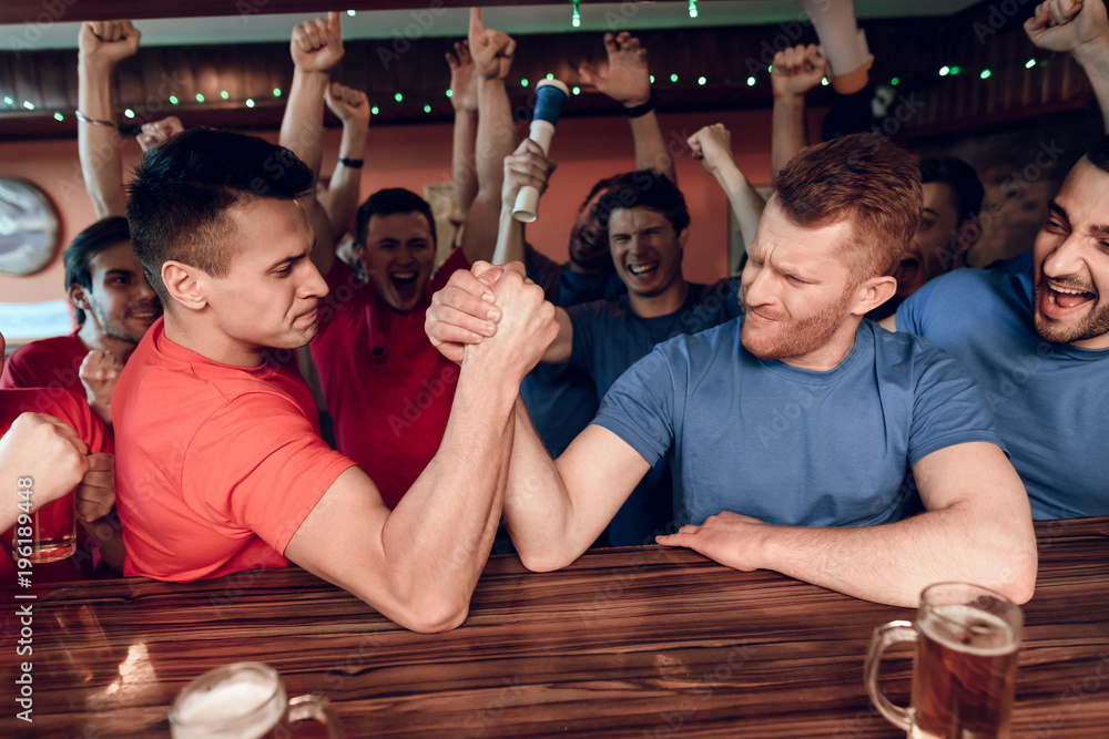 Blue and red team fans arm wrestling at sports bar with fans in ...