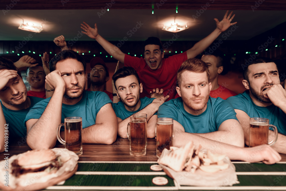 Sad blue team fans at bar in sports bar with red team fans celebrating ...