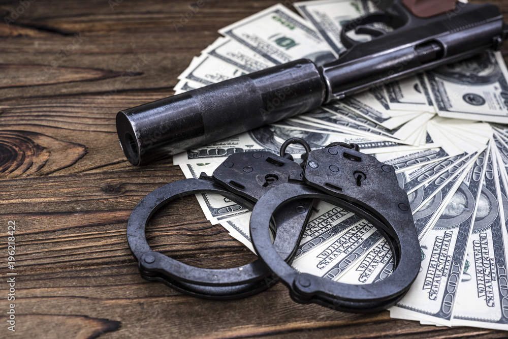 a pistol with a silencer, handcuffs, lies on a dollar money banknote ...