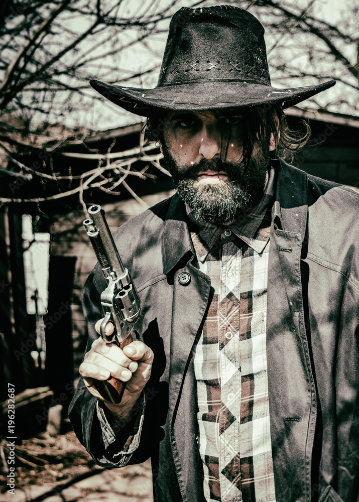 Cowboy holding up a gun, standing outside in an old west, western scene ...