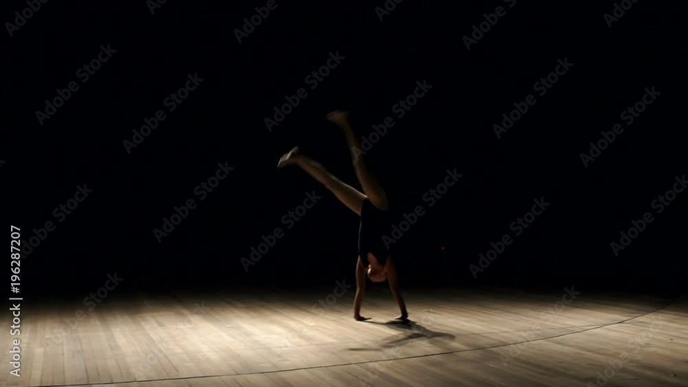 Little girl gymnast doing a somersault in the studio on a black ...