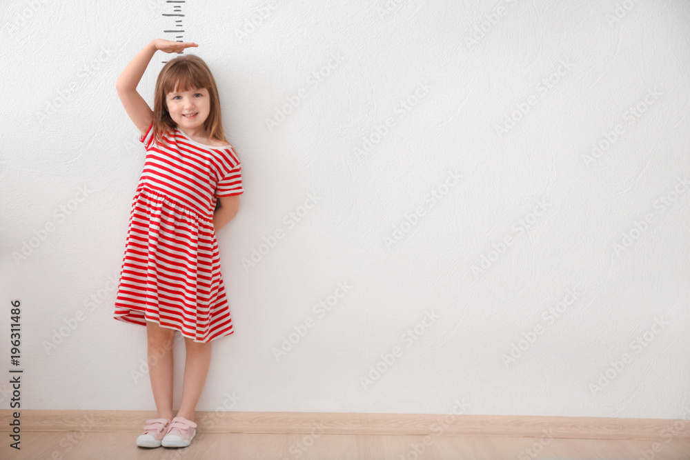 Cute little girl measuring height near light wall Stock Photo | Adobe Stock