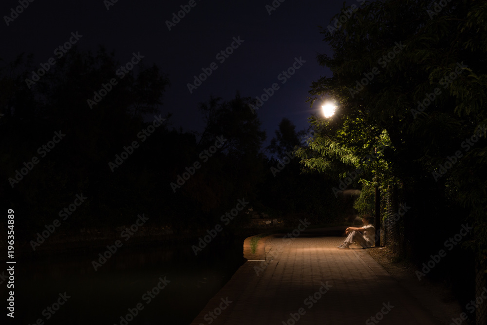Double exposure night scene of man sitting in the dark street under ...
