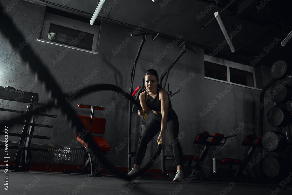 Young woman doing strength training using heavy ropes at the gym ...