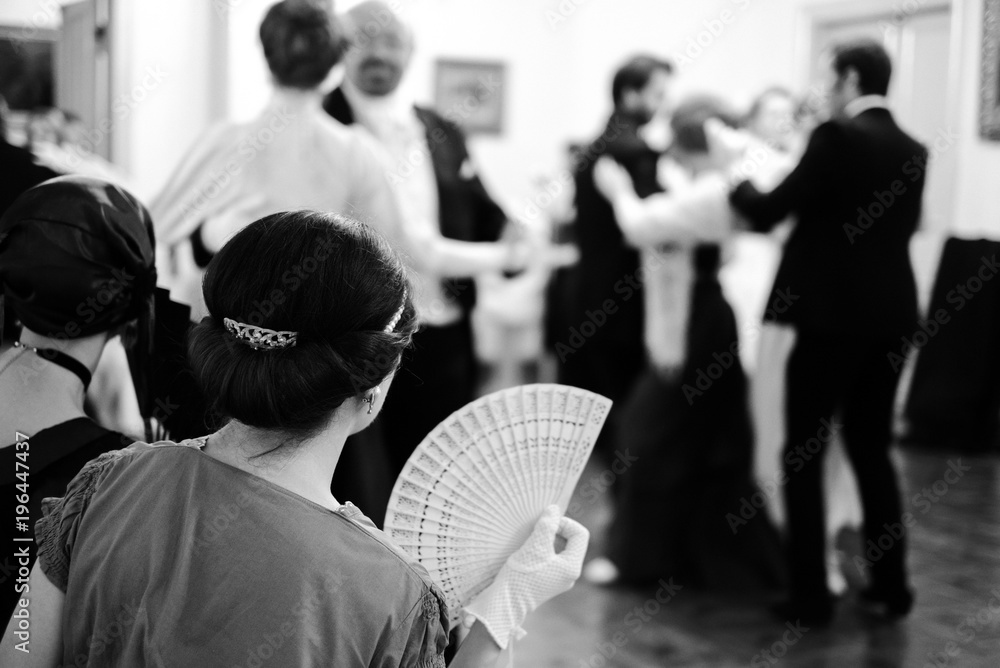 Two women in vintage dresses with fan in hands sitting at ball and ...