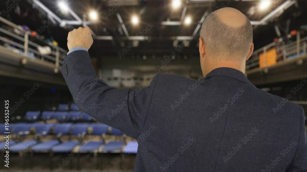 Man moving clenched fist up on repetition in empty hall back view ...
