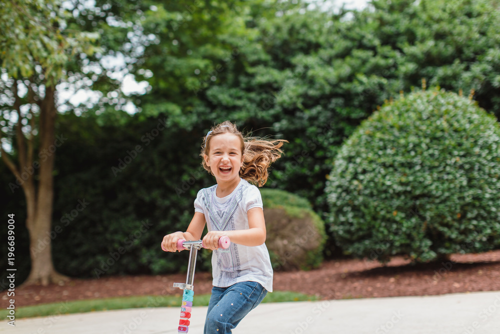 Cute young girl riding a scooter in her driveway Stock Photo | Adobe Stock