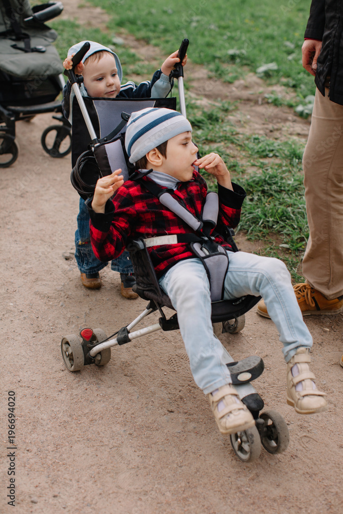 Little boy pushing stroller with his older brother with infant cerebral ...
